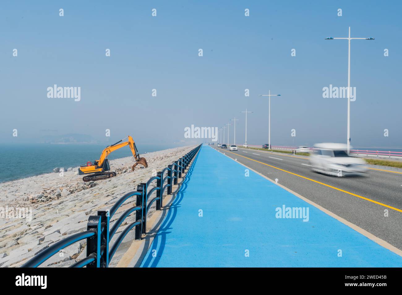 Backhoe sitting on ocean causeway next to blue concrete sidewalk on ...