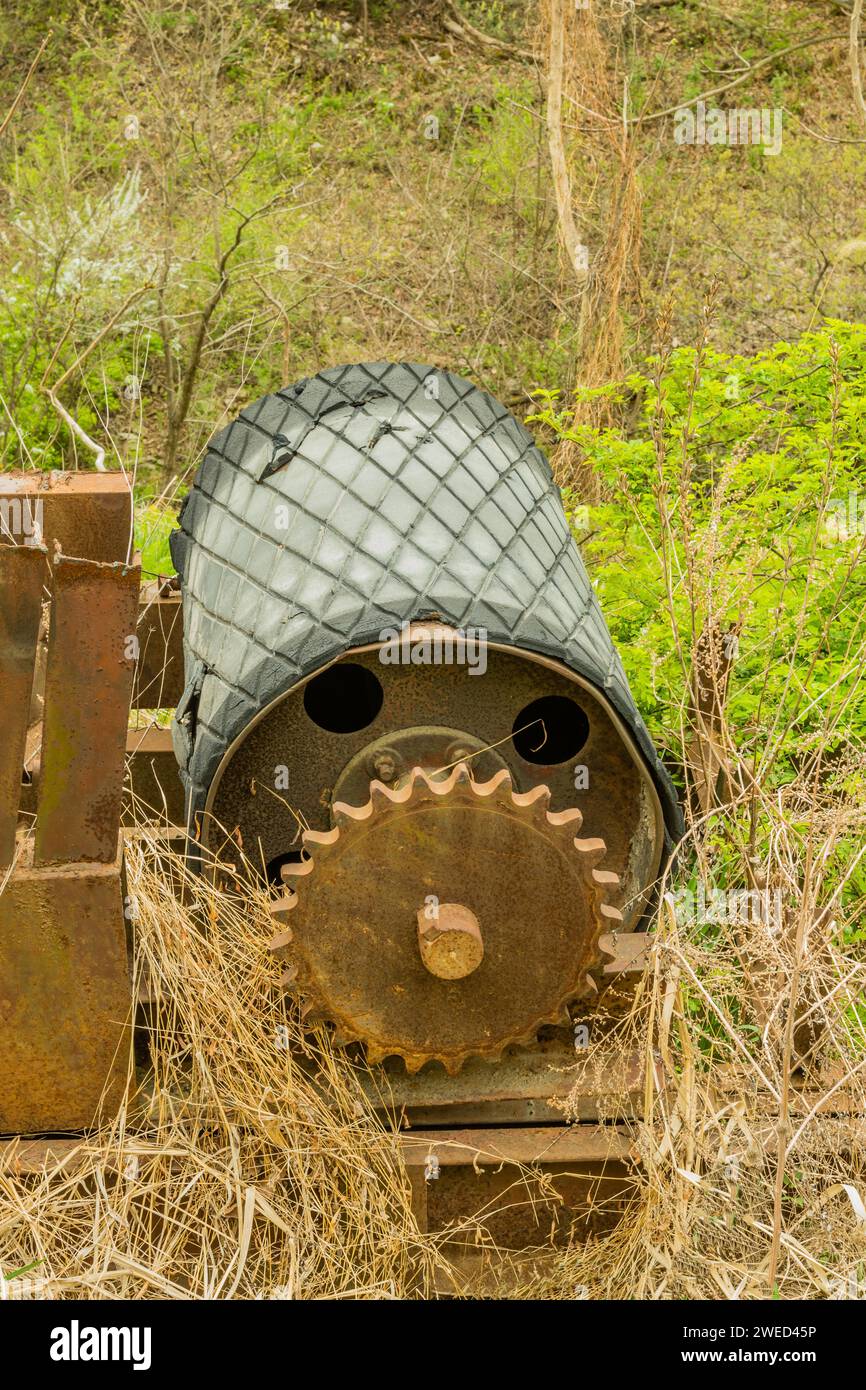 Discarded conveyor belt motor with chain sprocket laying in tall weeds ...