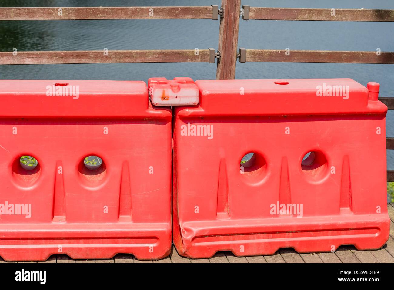 Two red plastic traffic barriers in front of fence on riverside ...