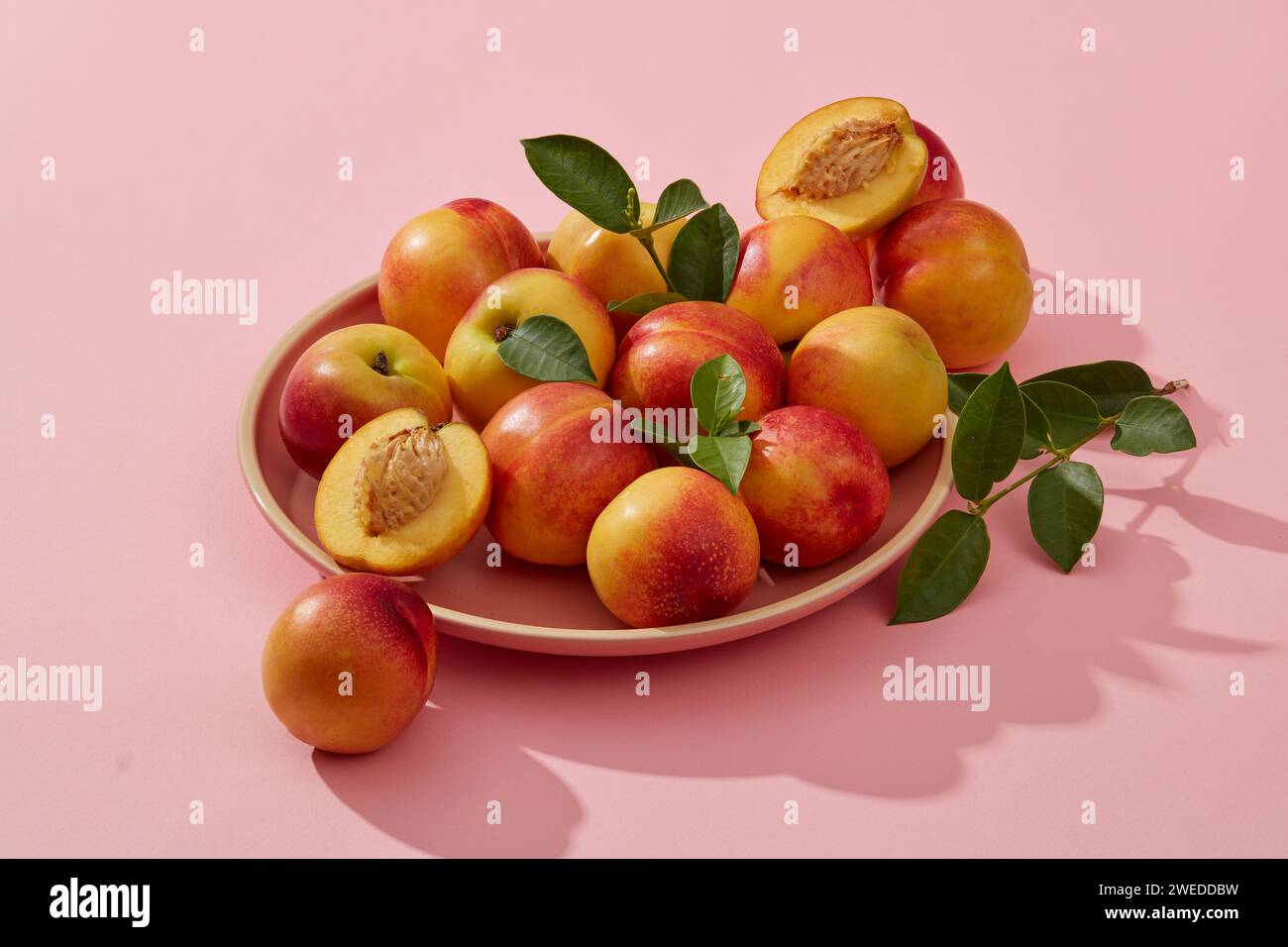 Against the pastel pink background, a dish of some peaches is displayed ...