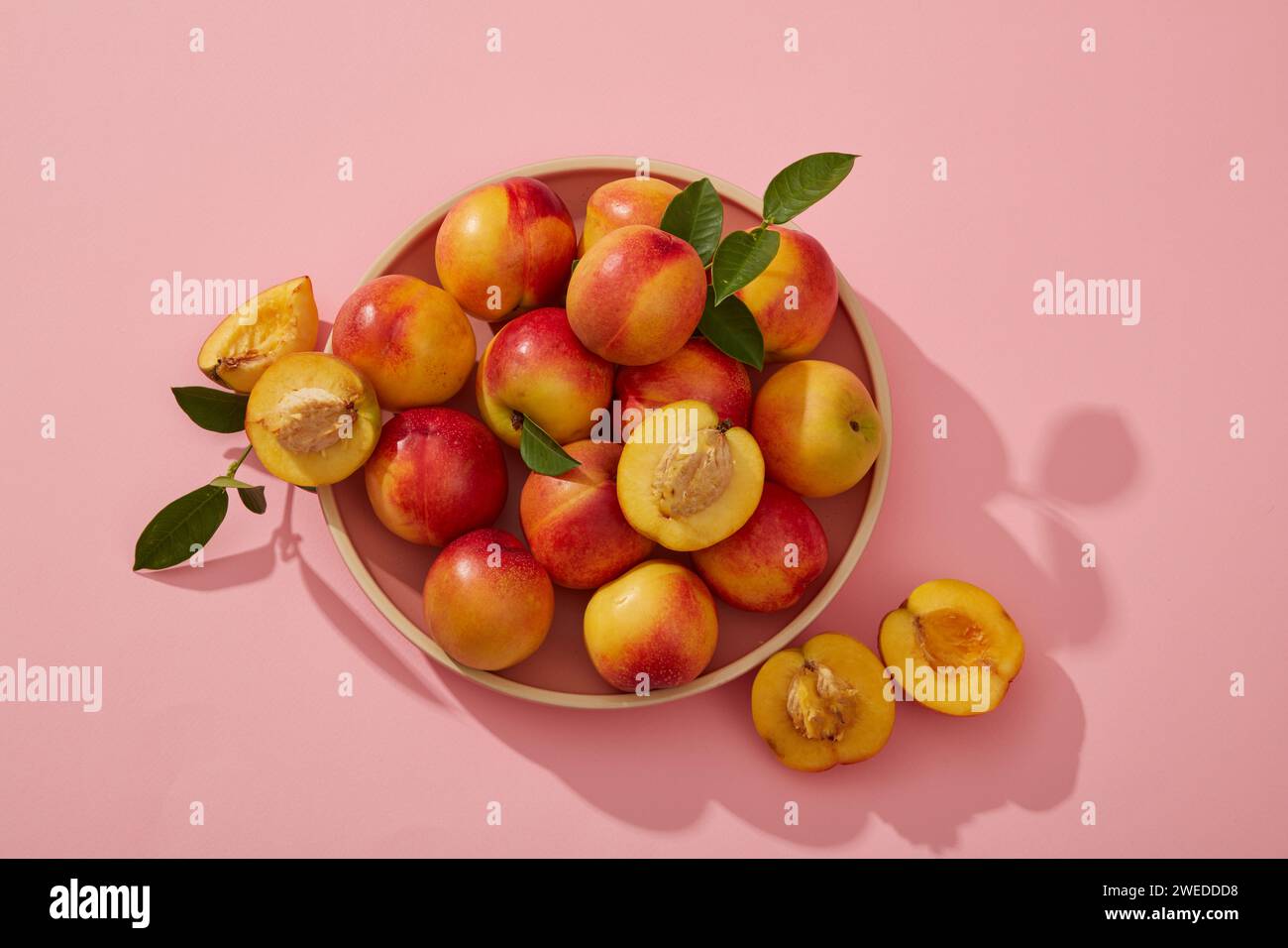 Flat lay of a dish in pink color containing many peaches, a peach cut ...