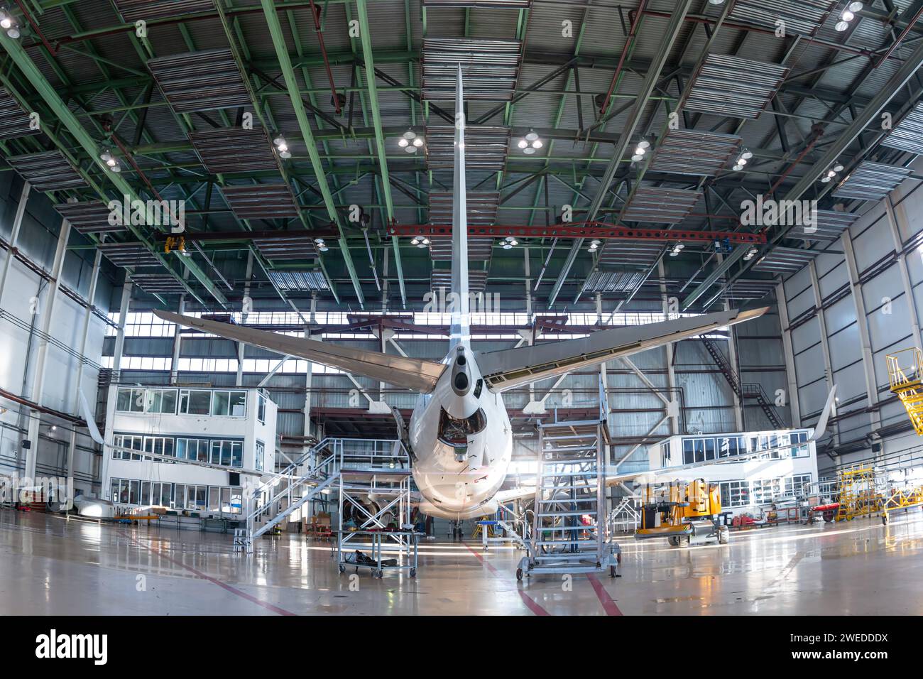 Rear view of a white passenger jetliner in the aviation hangar. Aircraft under maintenance ...