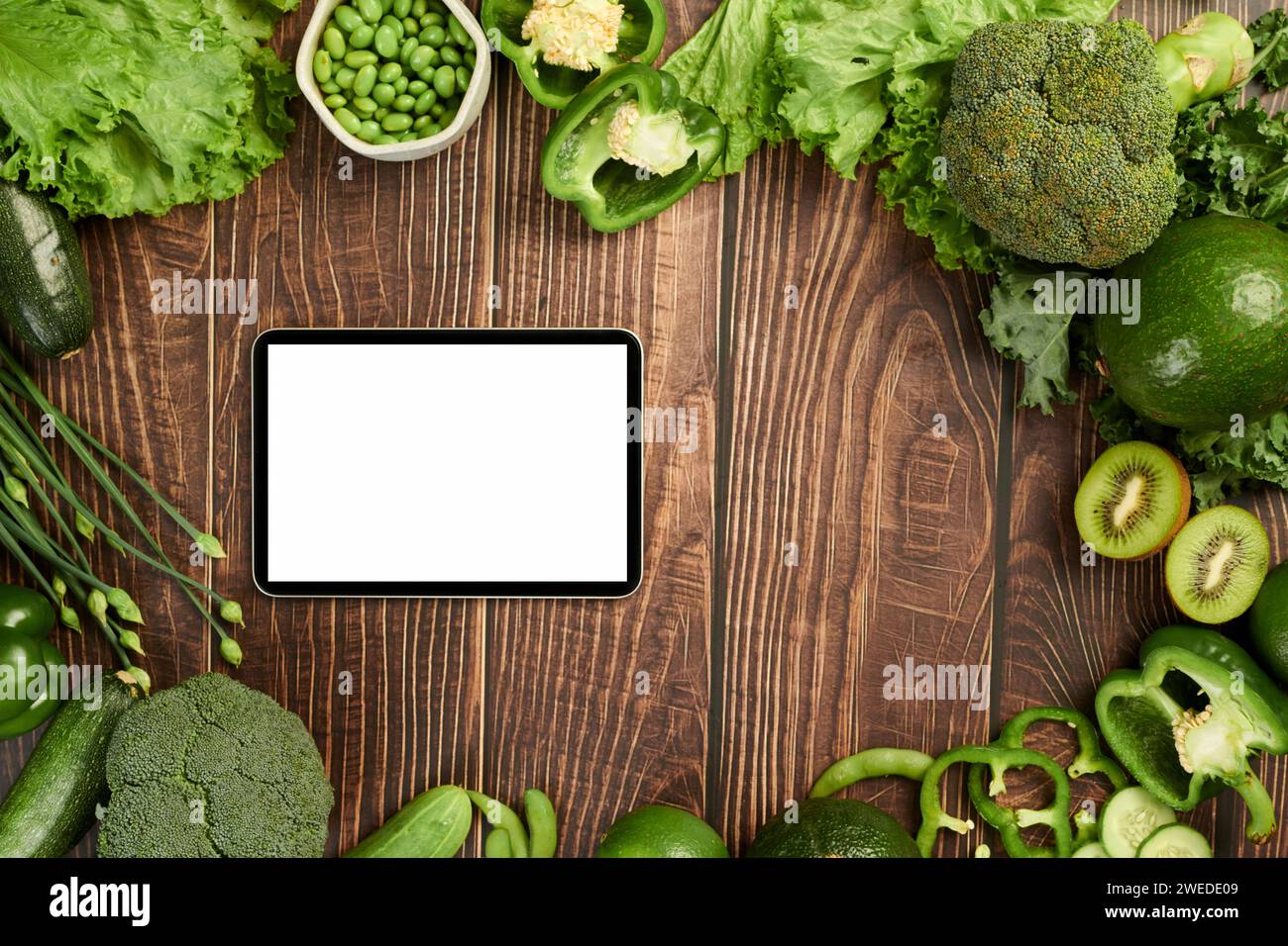 Digital table with white screen on wooden table with green fruits and ...