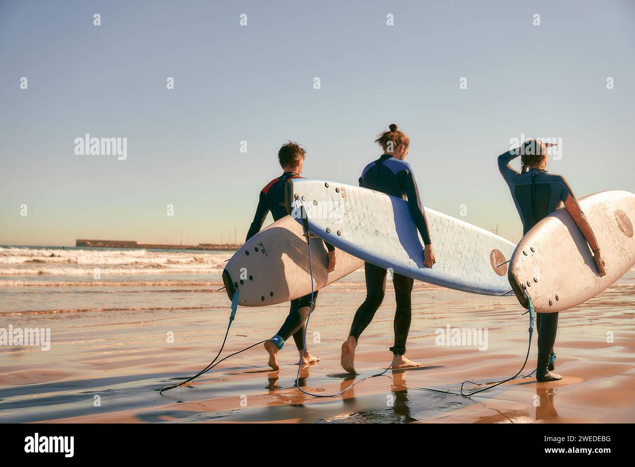 Back view of surfers with surfboards in wetsuit are walking on the ...
