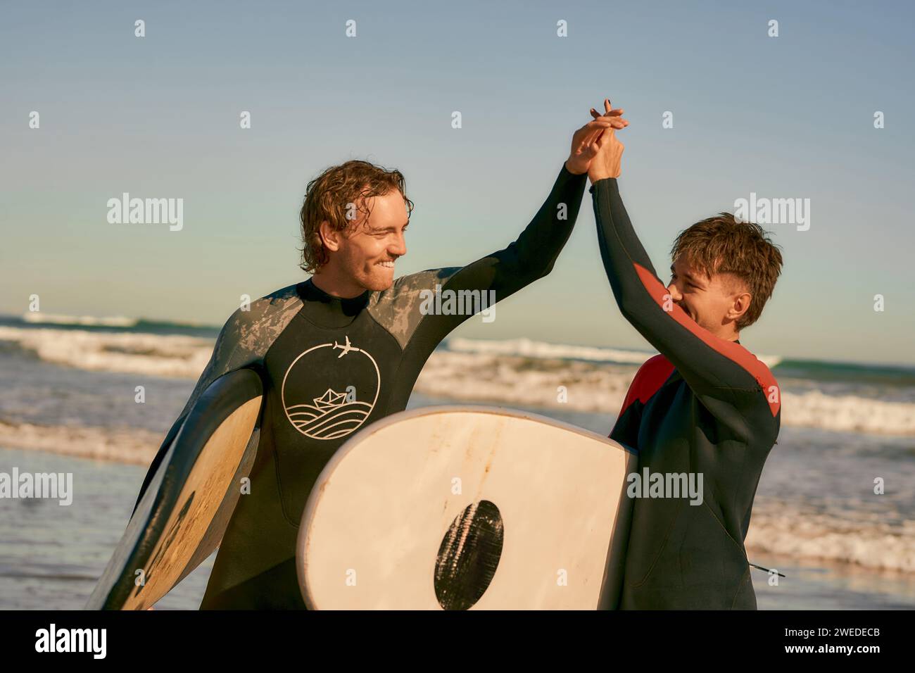 Two surfers greet each other by shaking hands before surfing on waves ...