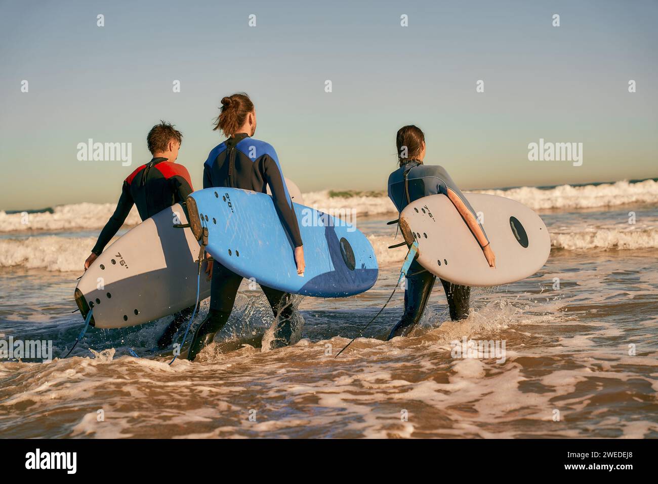 Back view of surfers with surfboards in wetsuit entering towards ocean ...