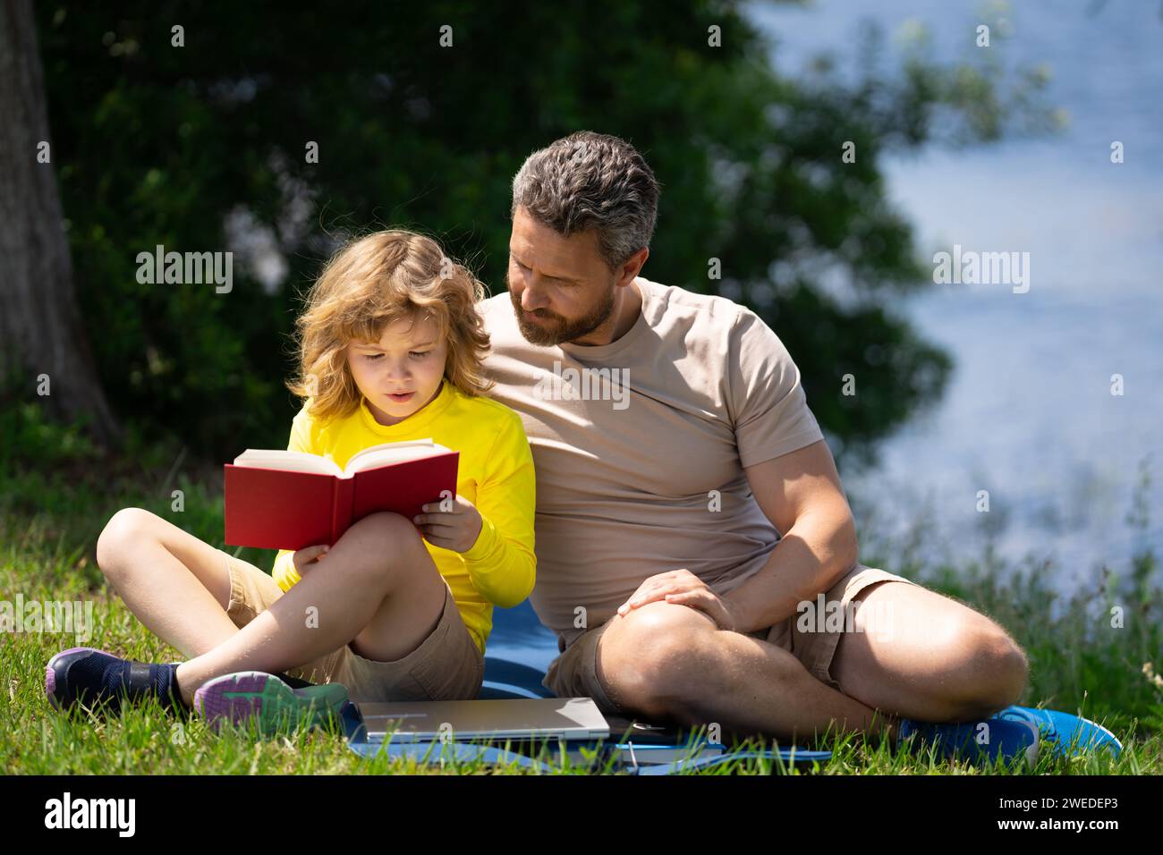 Outdoor school. Father and son reading book in park, man encourages boy ...