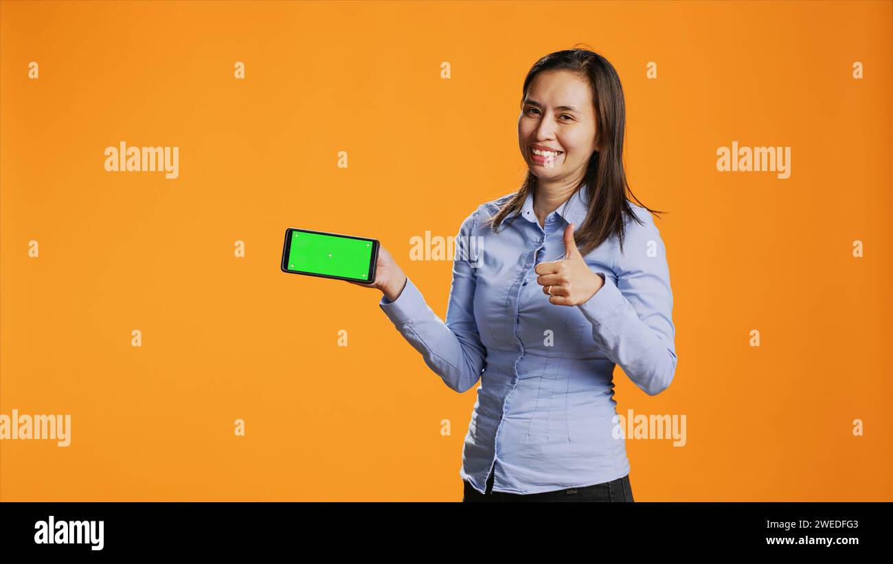 Confident girl shows greenscreen on phone display, standing over orange ...