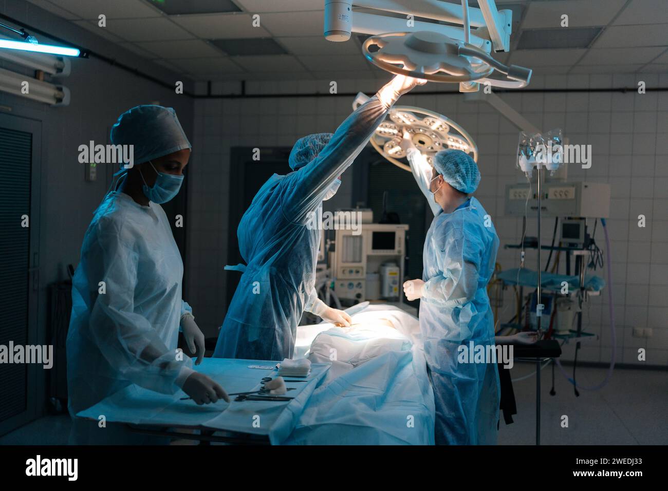 Remote view of doctor in surgical uniforms and masks adjusting light ...