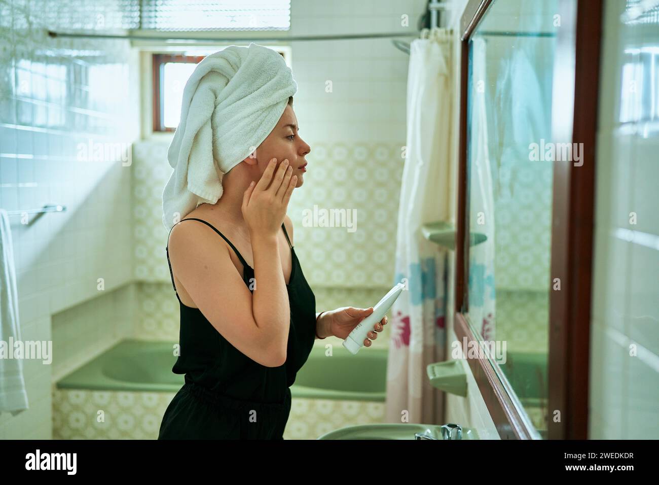 Woman in retro bathroom applies moisturizer to her face. Steps in front ...