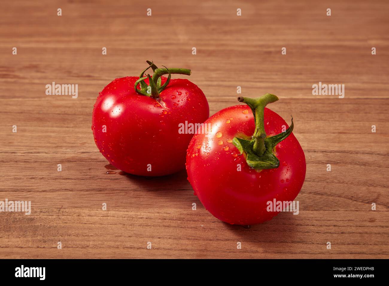 Two fresh-picked tomatoes with green stems are placed on a rustic ...