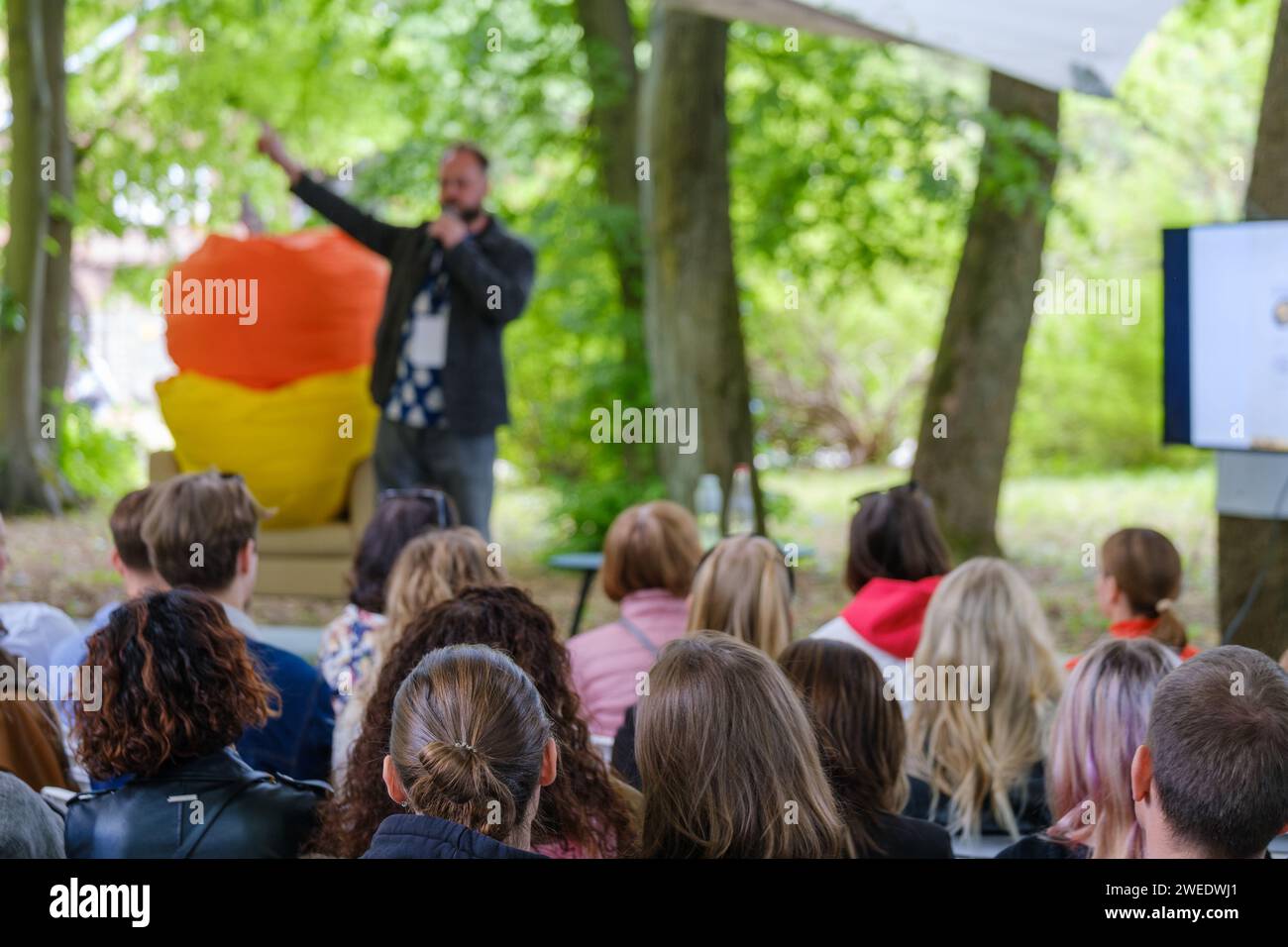 A speaker presents to an engaged crowd at an outdoor workshop in a lush ...