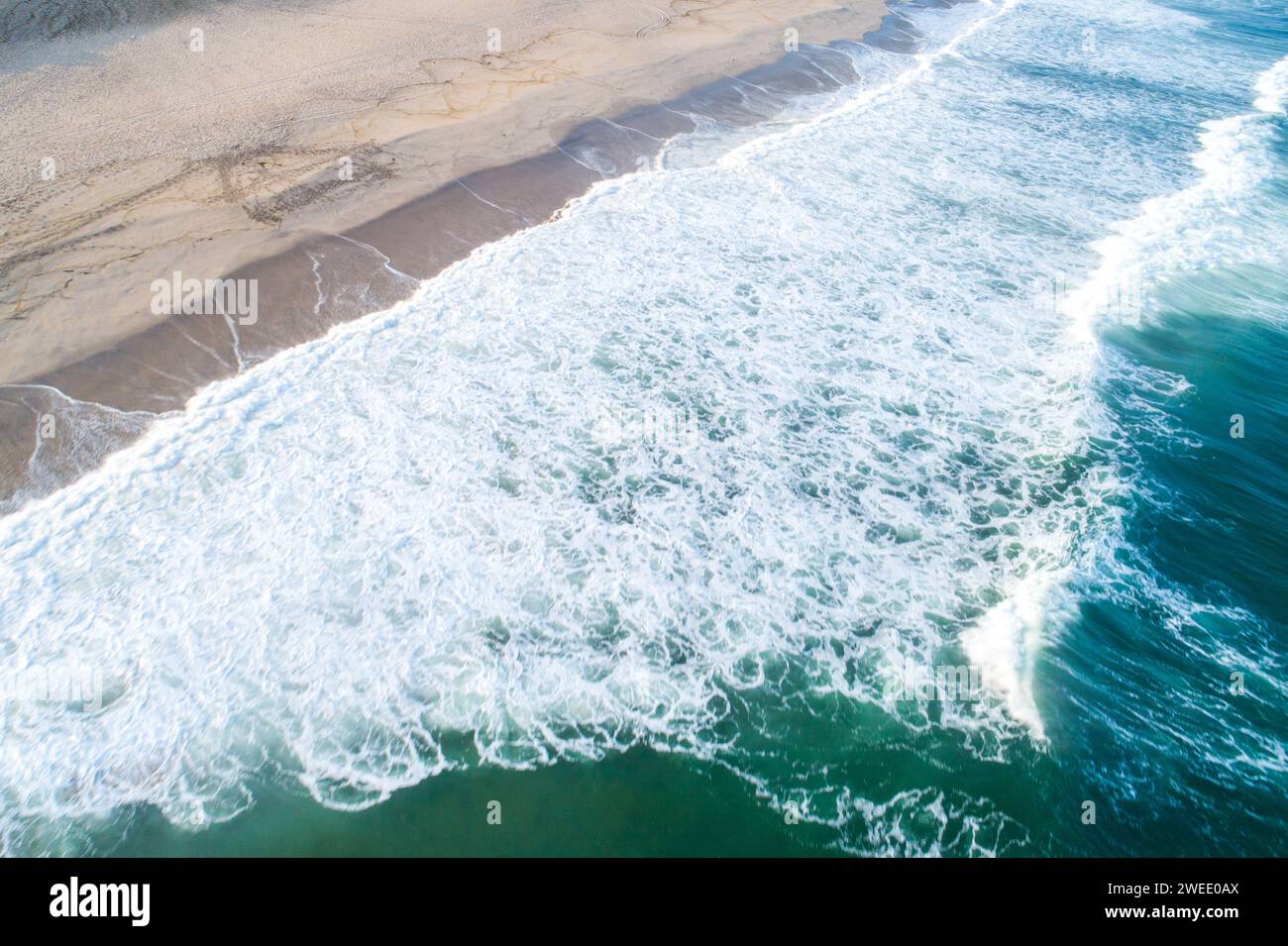 An aerial shot of the foamy waves of the ocean hitting the sandy shore ...