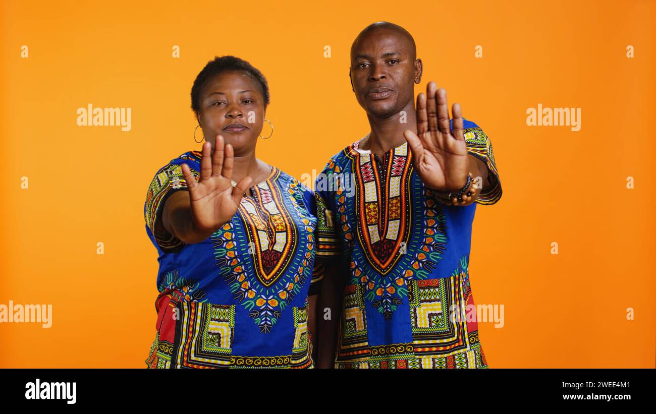 Confident ethnic couple showing stop sign in studio, raising palm and ...
