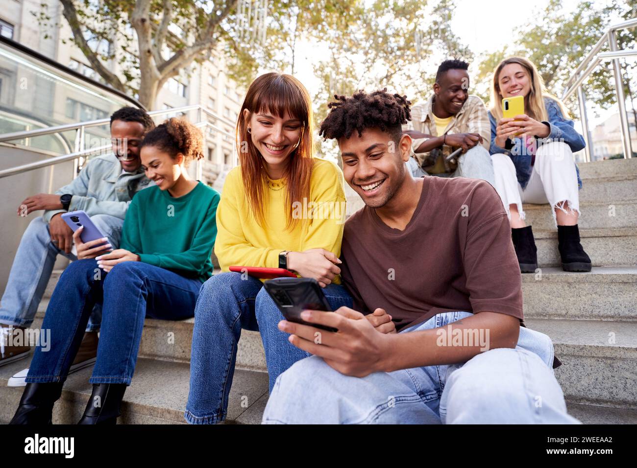 Multiracial group of young friends sitting on stairs hanging out, using ...