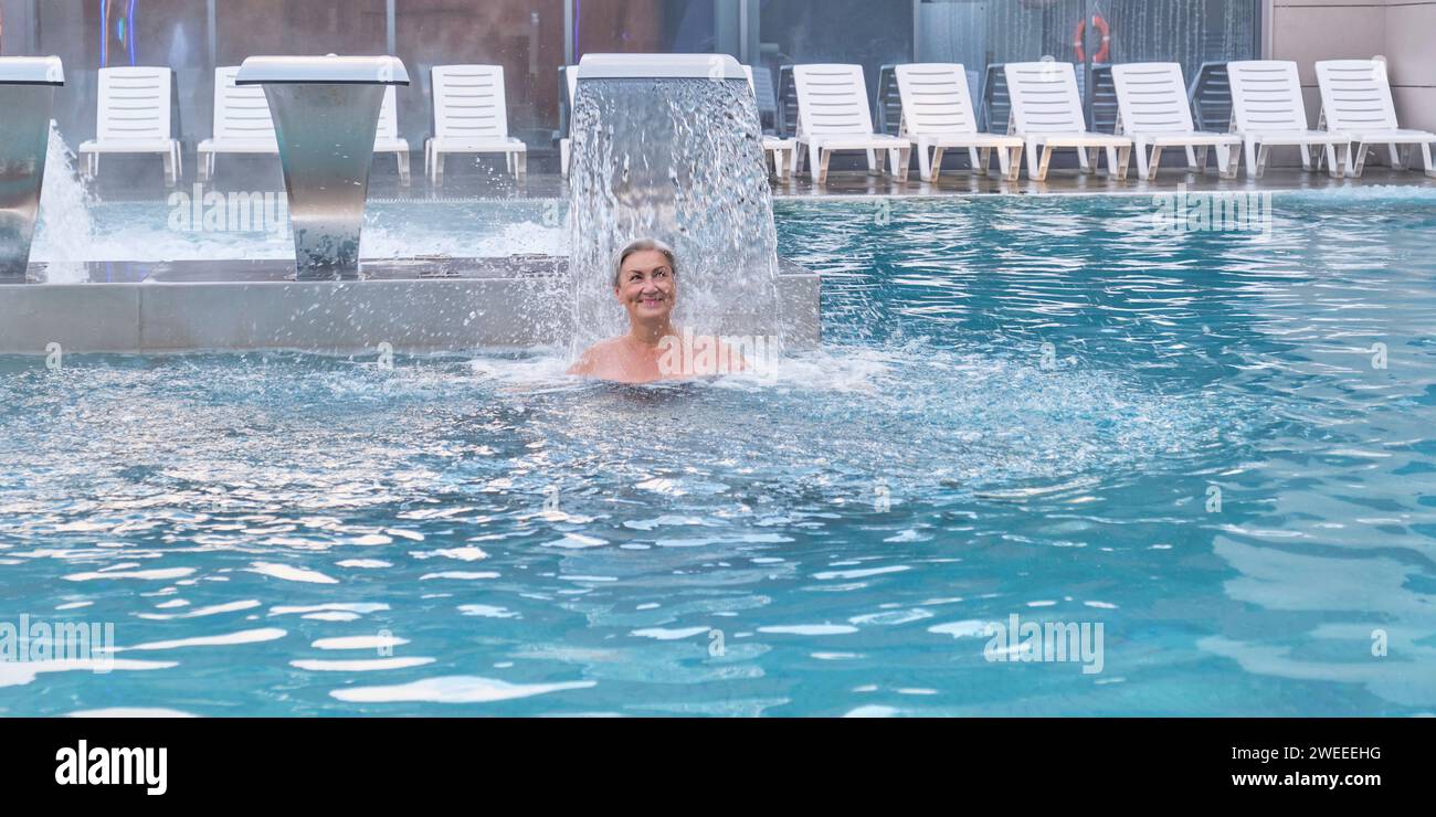 Senior caucasian woman enjoying falling jets of water in outdoor ...