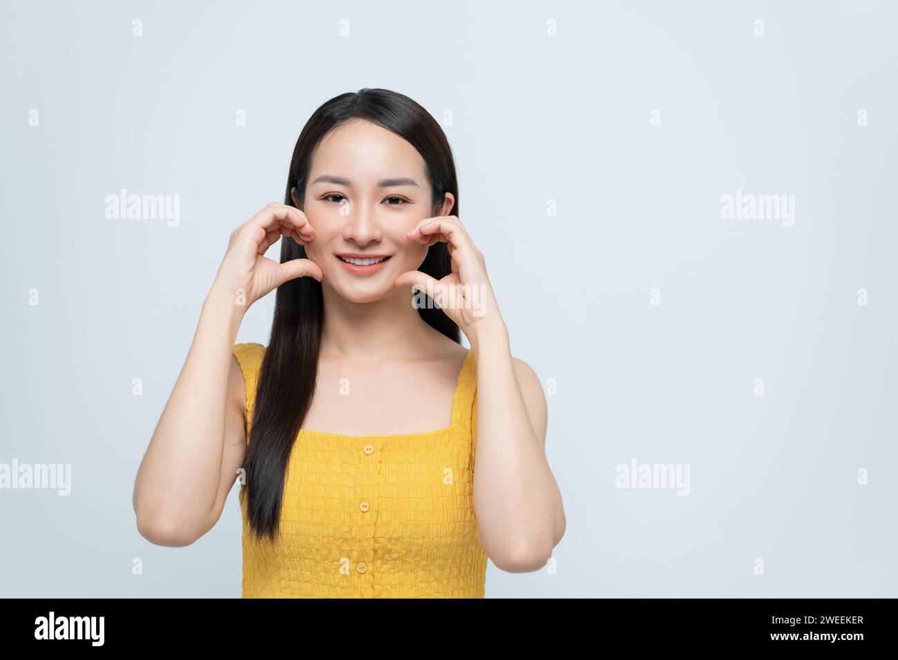 Beautiful young Asian woman making hand heart to her cheek on isolated ...