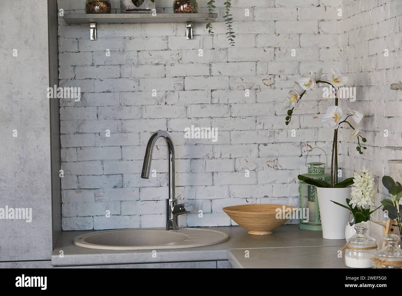 Trendy kitchen design featuring sink and greenery accents. White brick ...