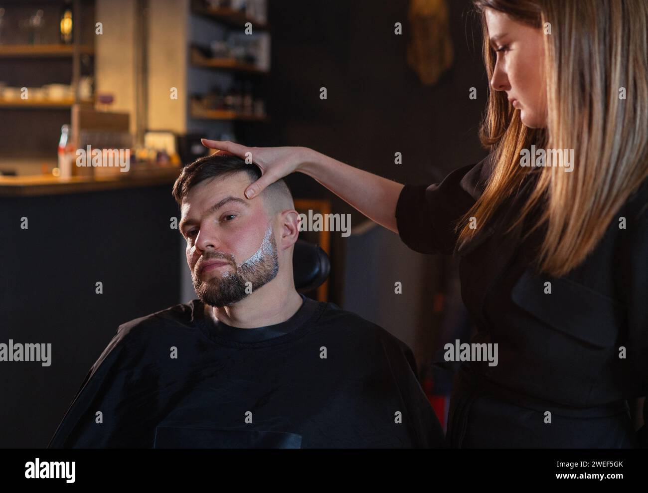 Long-haired young female Barber valuates bristle edges after straight ...