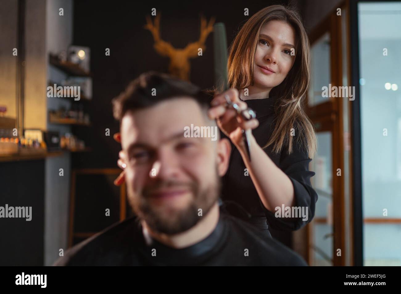Young female barber portrait evaluates her hairstyle work for smiling ...