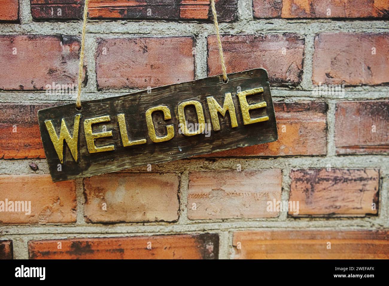 Welcome sign hanging on brick wall background Stock Photo - Alamy