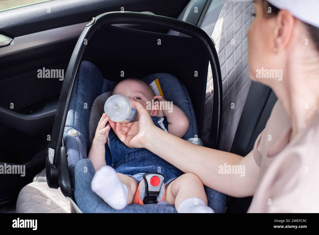 mother feeds the baby in, car seat in the car, milk from a bottle ...