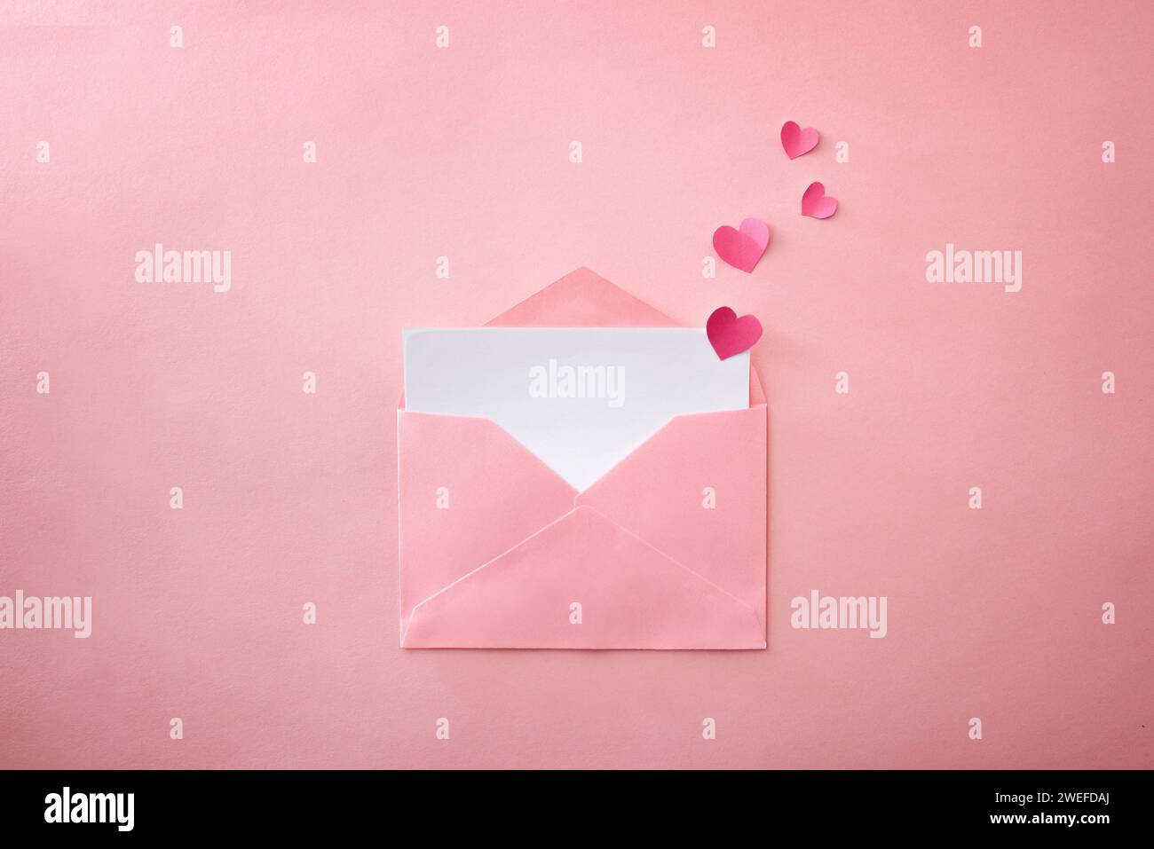 Open pink envelope with empty white sheet with heart cutouts coming out ...
