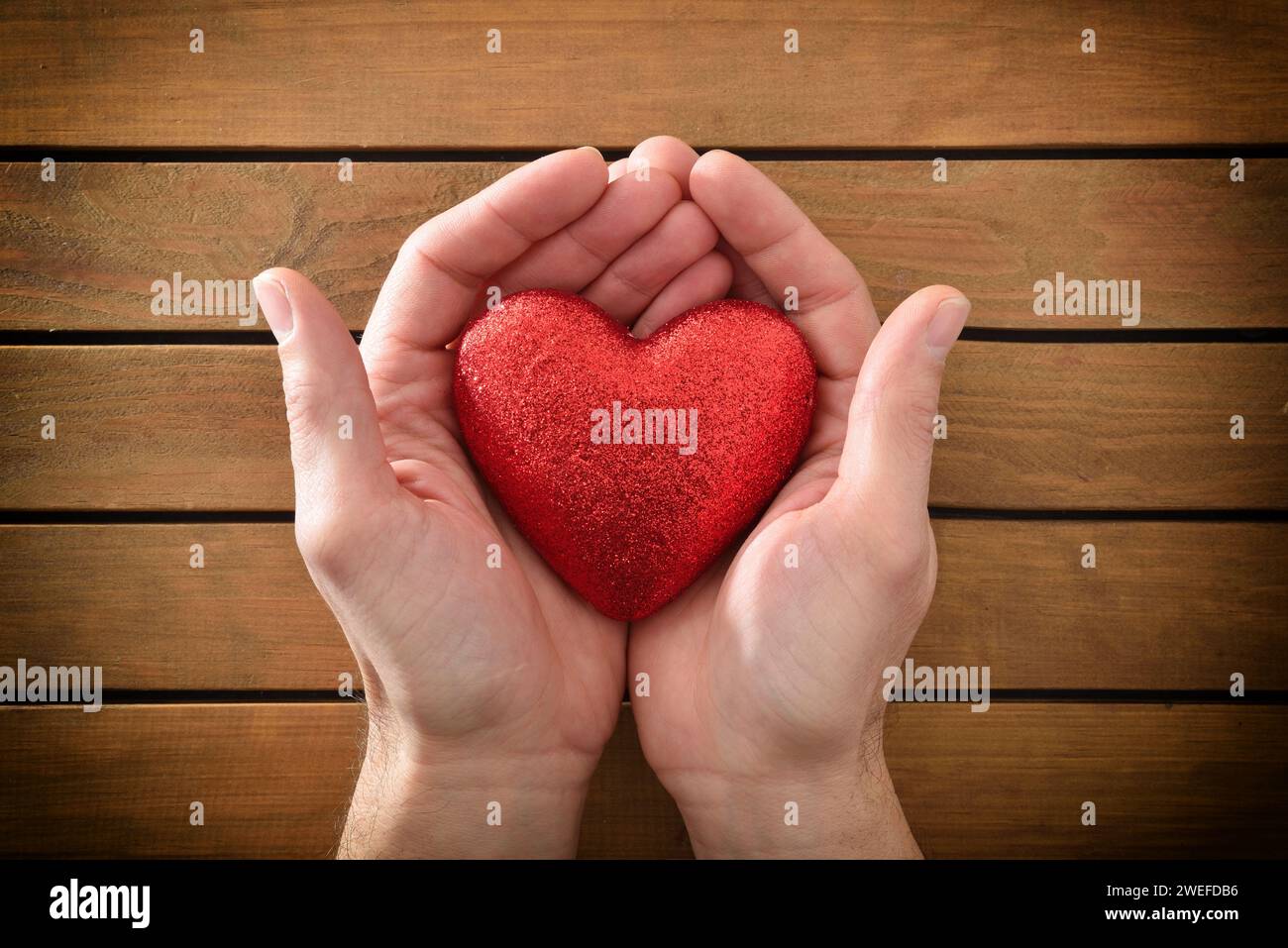 Glitter heart between a man's hands on wooden slatted table. Top view ...