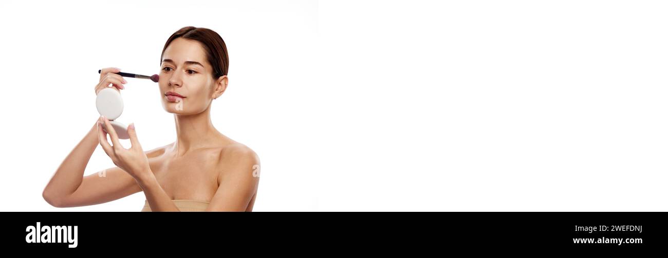 Pretty young woman with smooth spotless skin applying blush on cheeks ...