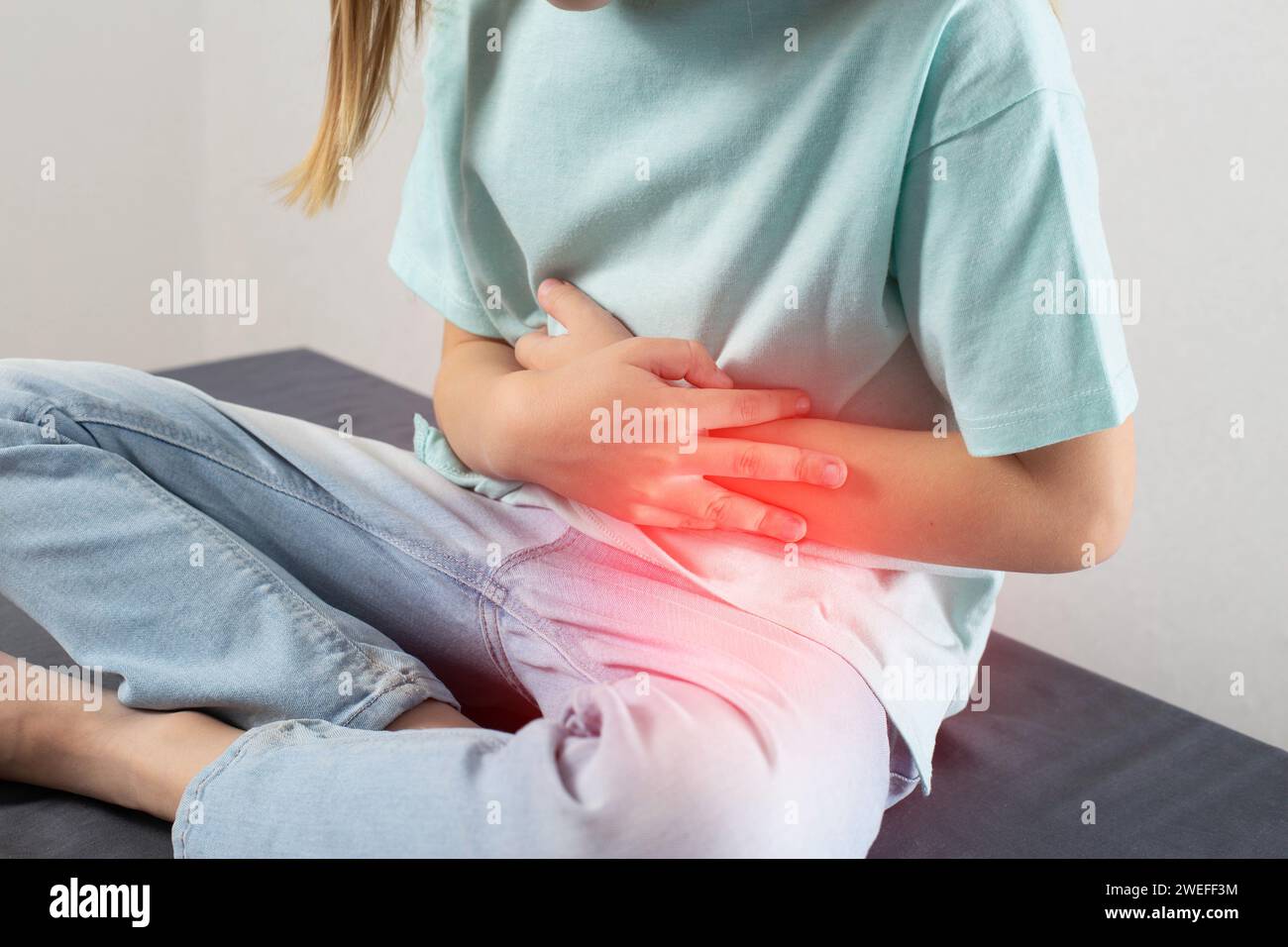 A little girl of seven years old sits and holds her red belly. Pain and ...