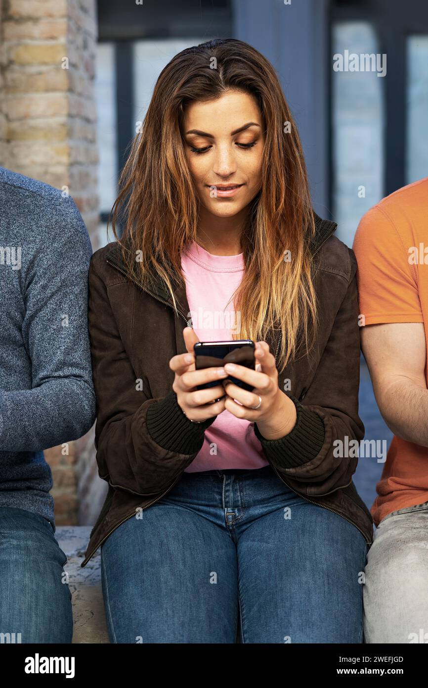 Focused young woman browsing smartphone, flanked by friends in urban ...