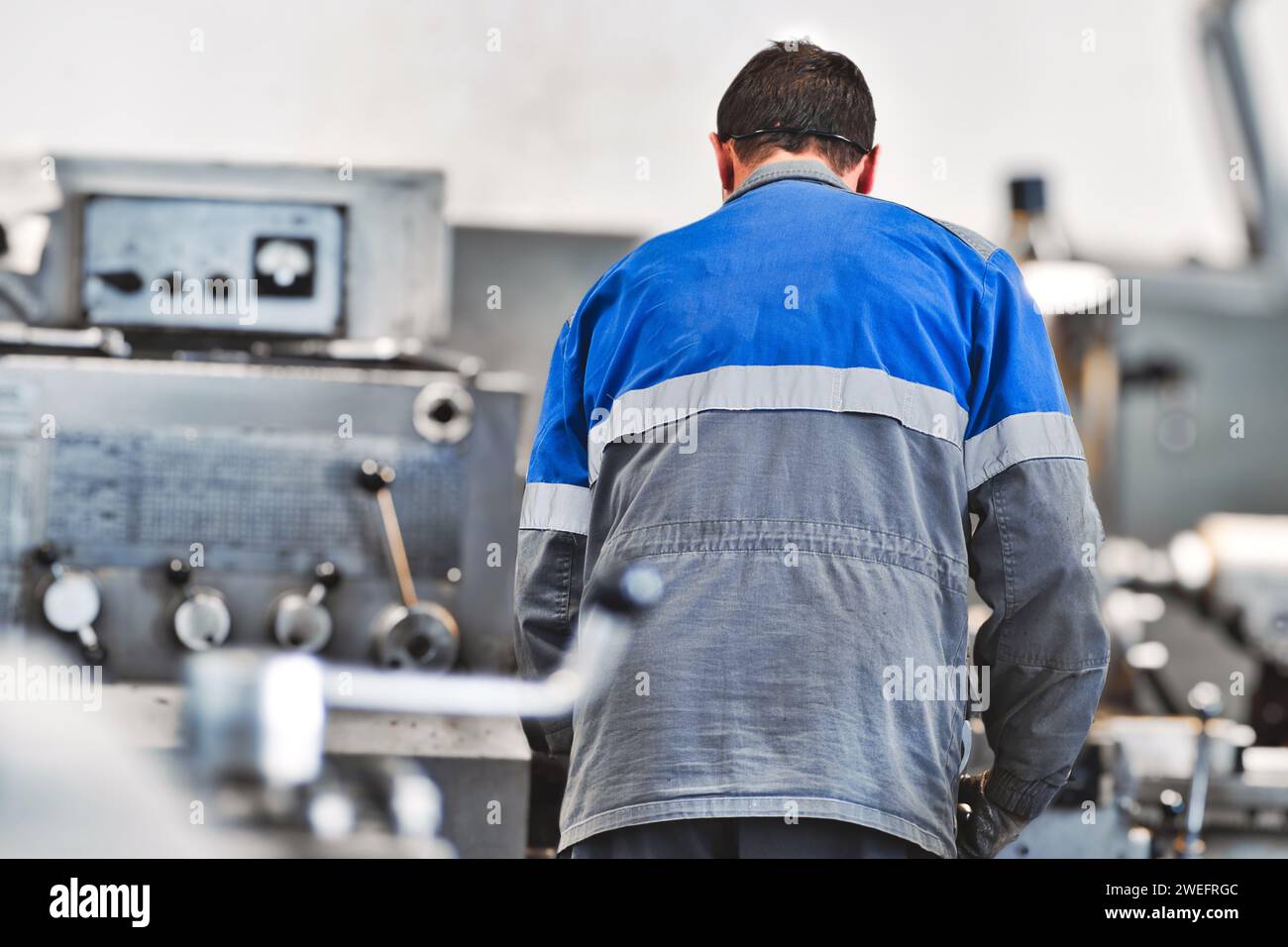 Turner in overalls works at lathe in turning shop at factory. Elderly ...