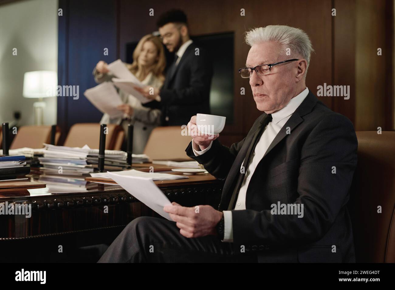 Mature lawyer sitting and reading document while drinking coffee, his ...