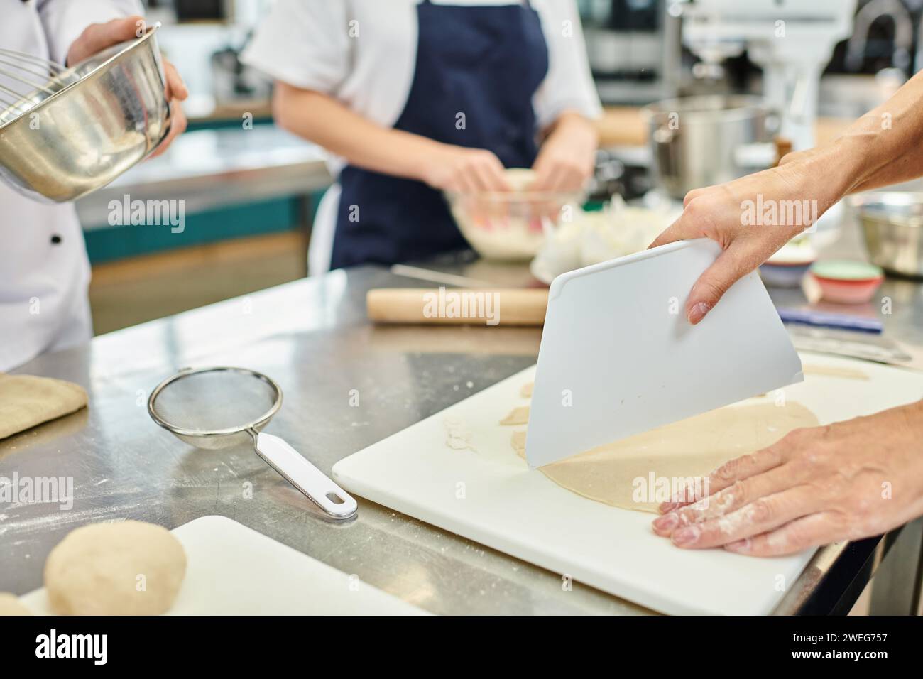 cropped view of mature woman cutting dough next to her young colleague ...