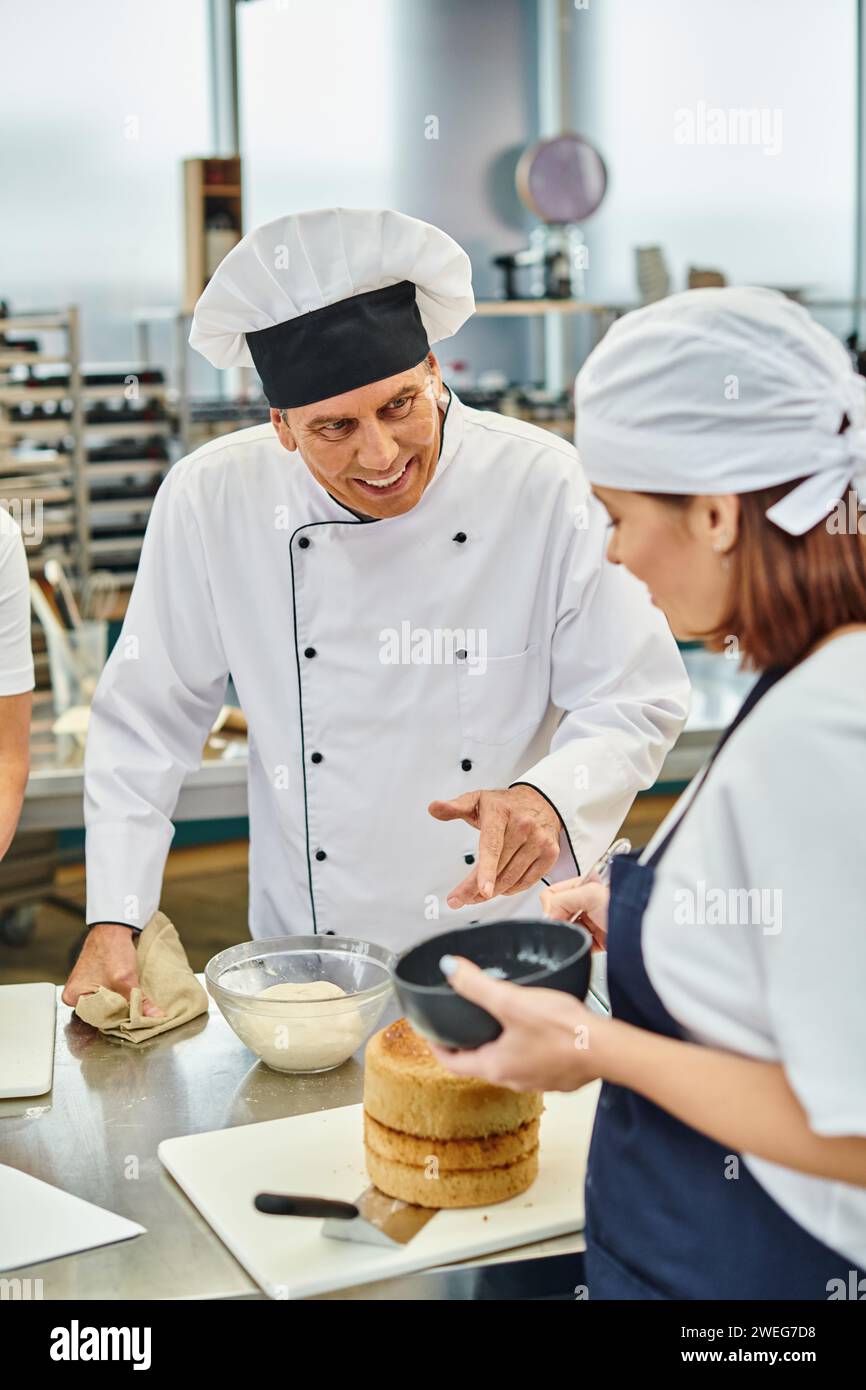 focus on mature chief cook in white hat talking to young blurred chef ...