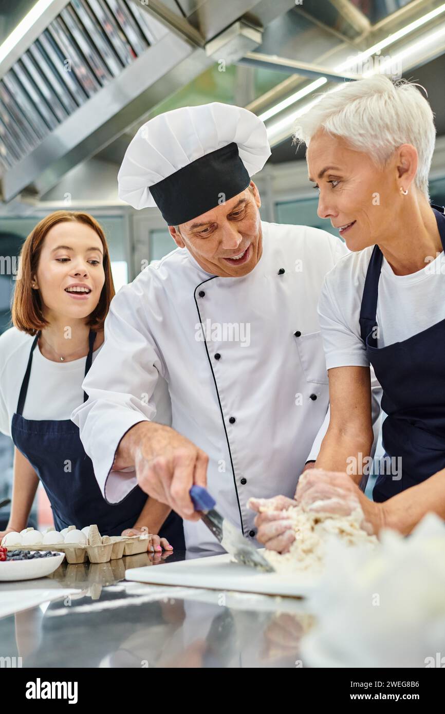 cheerful mature chief cook in white hat helping his jolly female chefs ...
