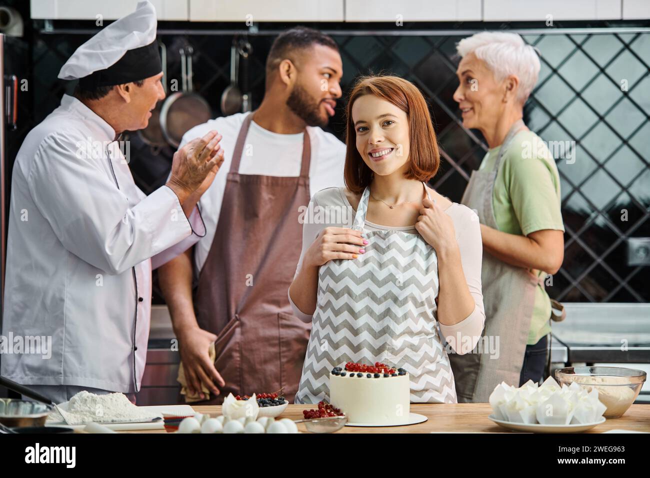 young jolly woman in apron looking at camera next to cake with her ...