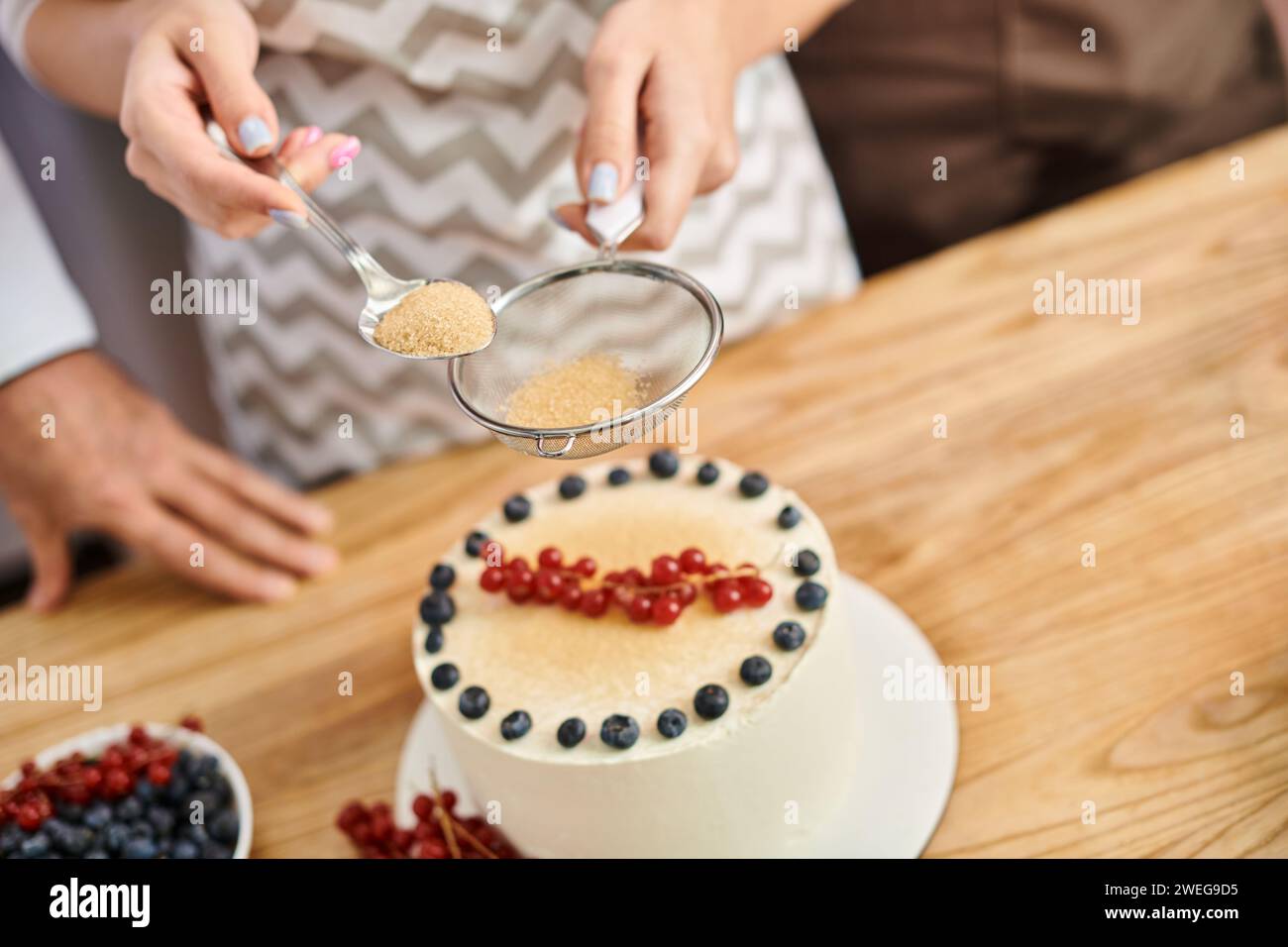 young woman with nail polish decorating delicious cake next to chef ...