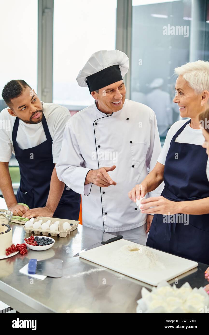 joyful mature chief cook smiling at his interracial chefs while they ...