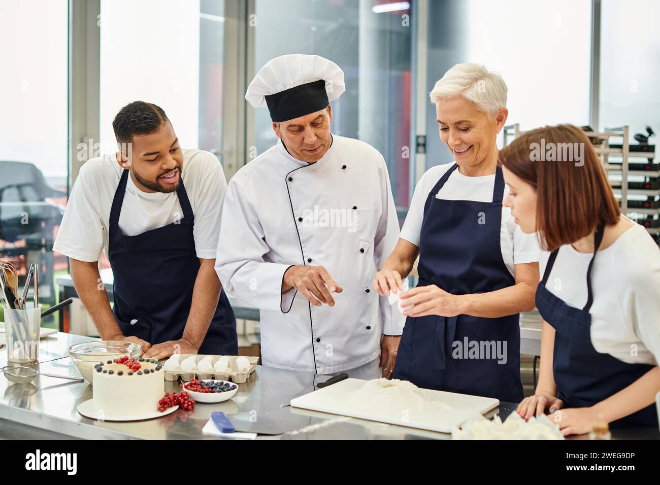 cheerful mature female chef breaking egg next to her young colleagues ...