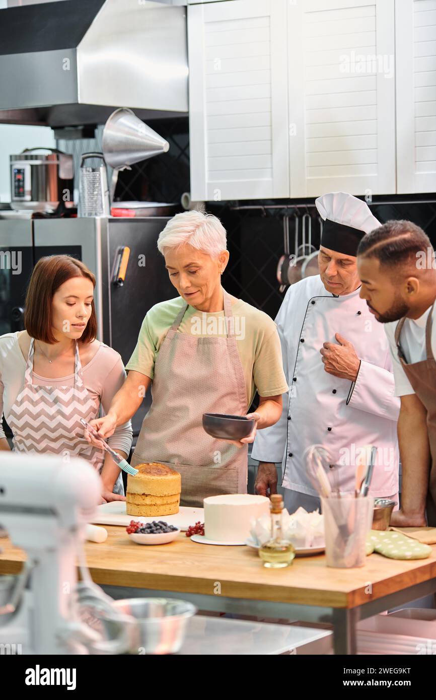mature woman in apron brushing cake with syrup on cake next to diverse ...