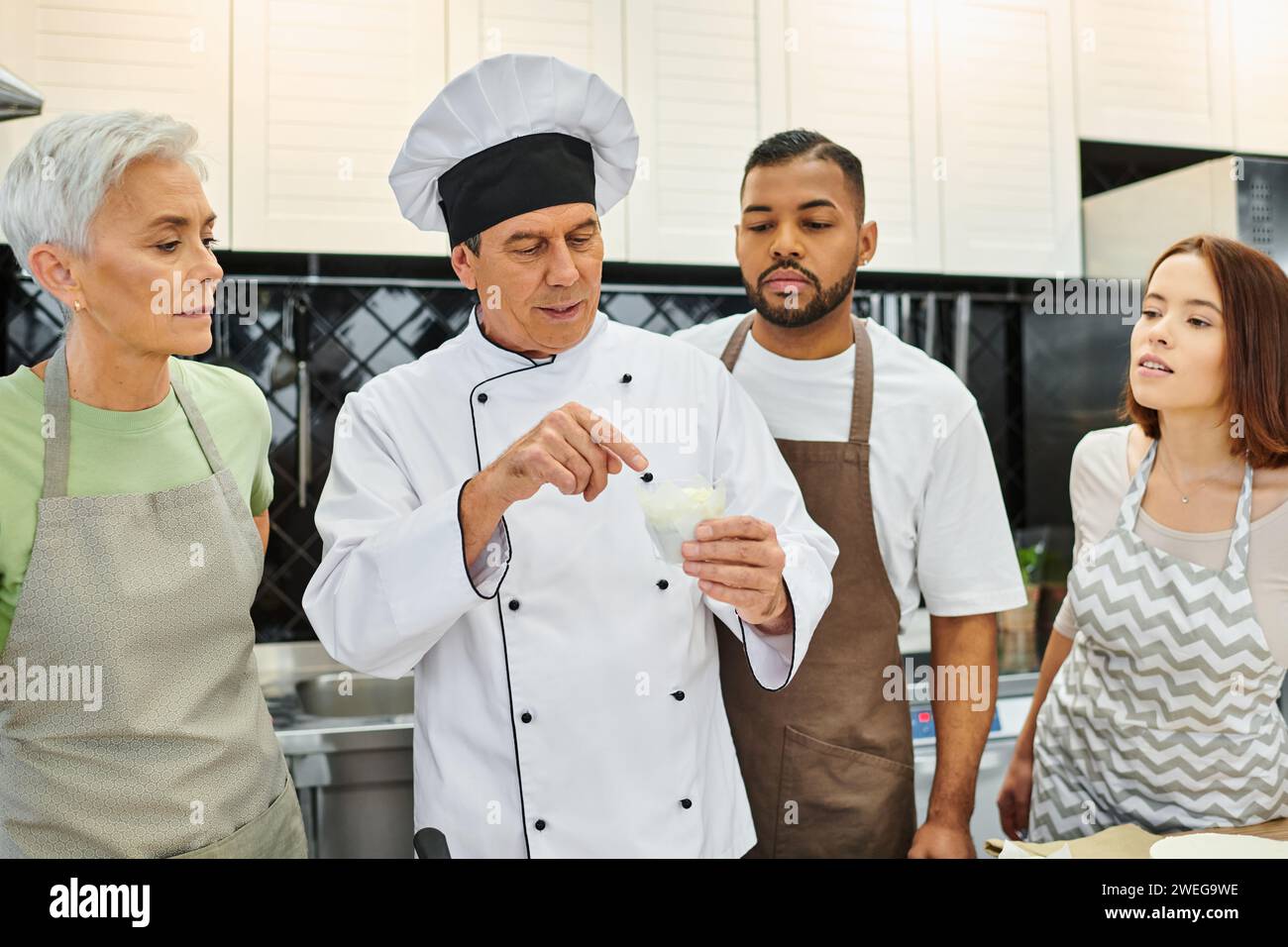 good looking mature chef discussing with his multiracial students how ...