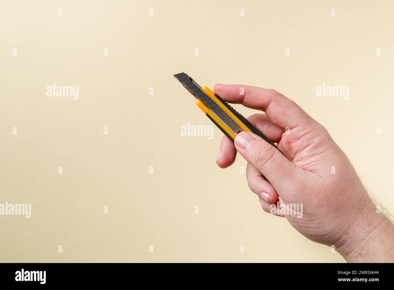 Hand holding a yellow and black metal utility knife in front of a ...