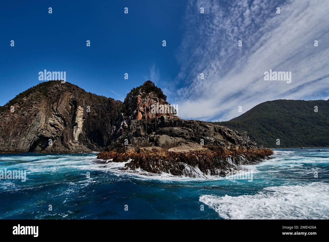 Rocky island in turquoise water with a cave, surrounded by a rock wall ...