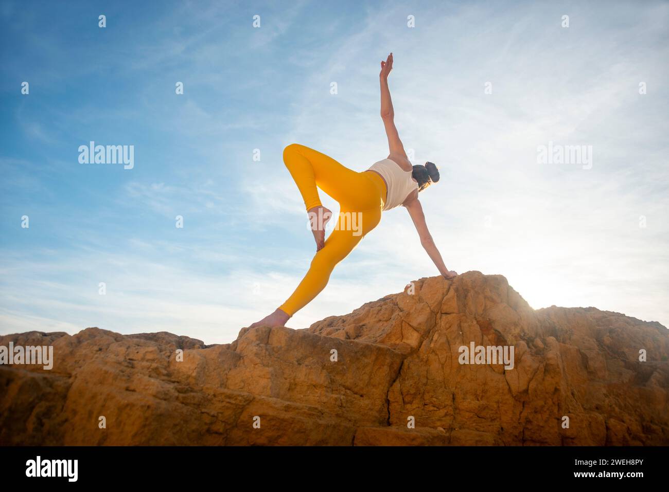 fit woman doing a side plank yoga pose on a rock, blue sky background ...