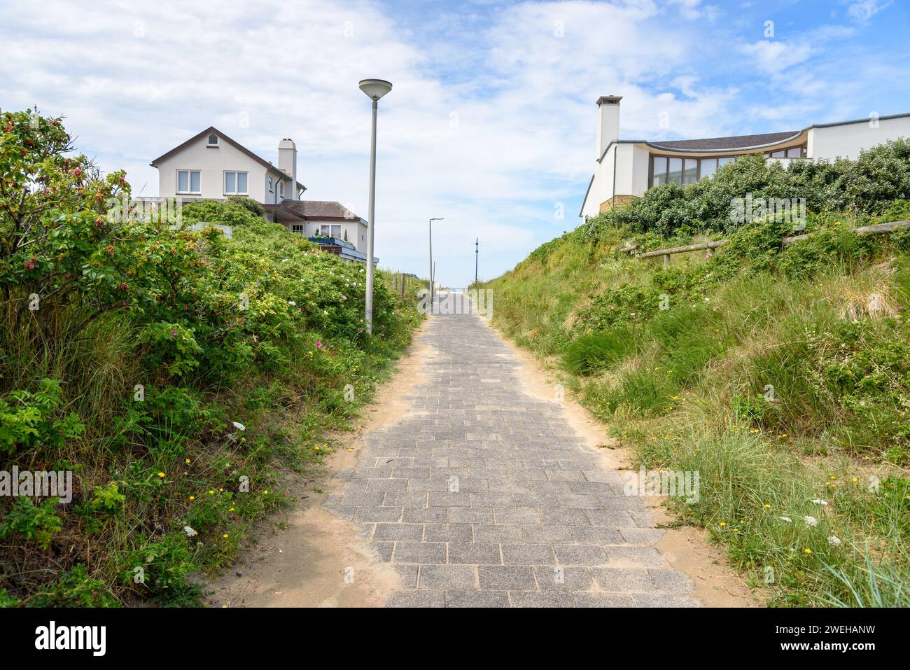 Empty footpath between two modern houses leading to a beach on a partly ...