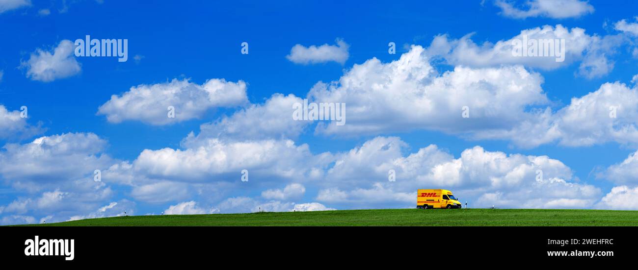 a DHL delivery van on a country road in the middle of meadows with blue ...
