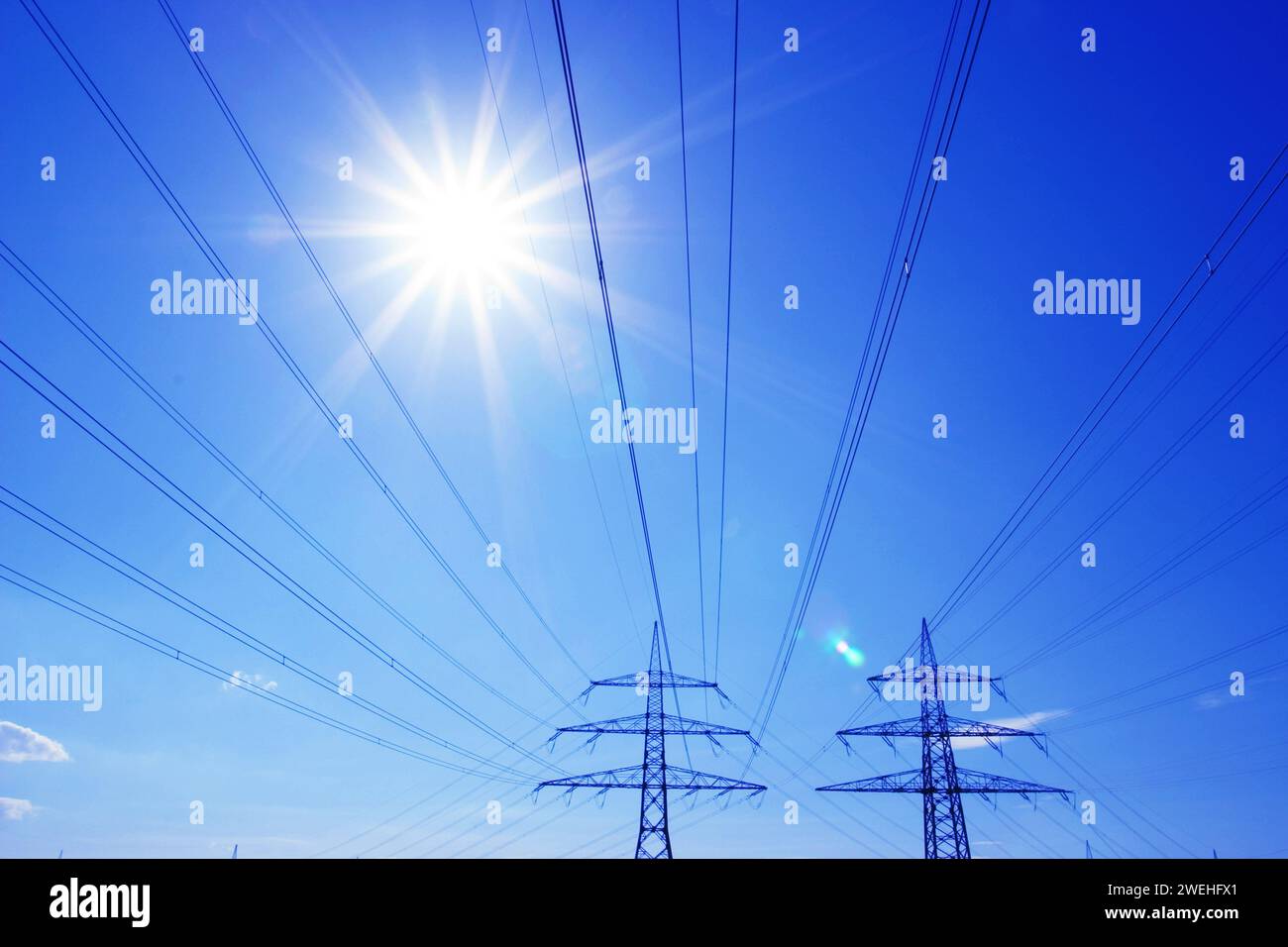 Two high-voltage pylons with high-voltage lines backlit by blue sky and ...
