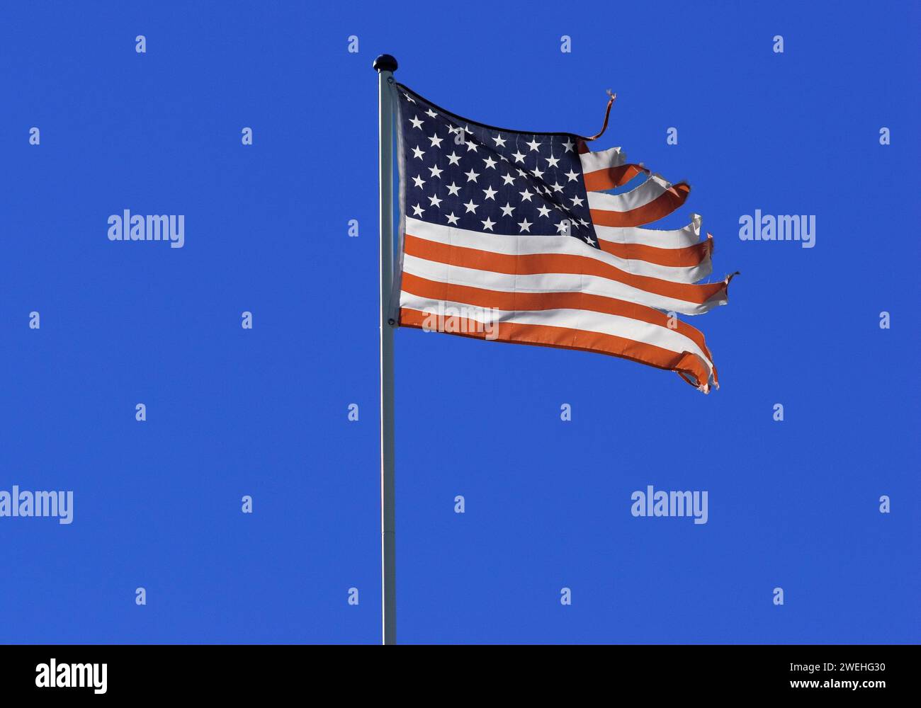 a faded and torn flag of the USA flies in the wind against a blue sky ...