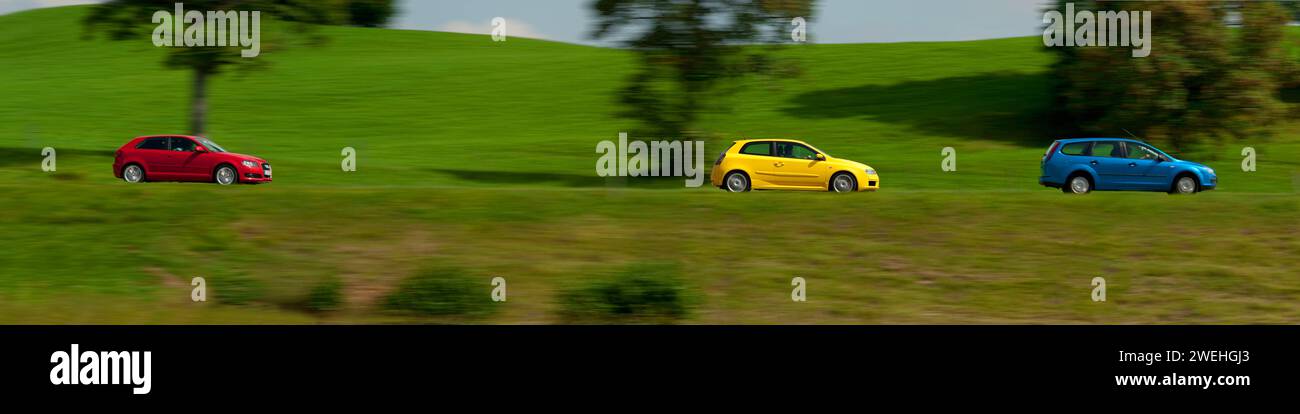 a blue, yellow and red car driving through a green landscape near Bad ...